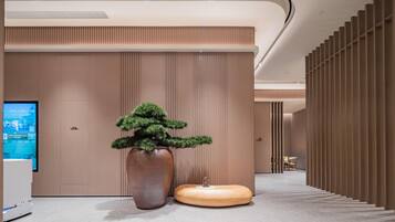 Um interior moderno com uma grande árvore bonsai em vaso, um banquinho de madeira e uma tela digital na parede.
