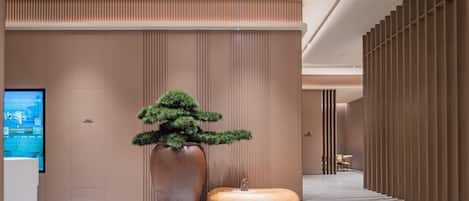Um interior moderno com uma grande árvore bonsai em vaso, um banquinho de madeira e uma tela digital na parede.