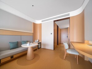 Quarto de hotel moderno com sofá, mesa redonda, escrivaninha e uma cadeira.