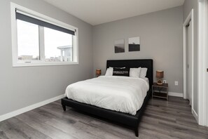 Quarto moderno com uma cama grande, uma mesa de cabeceira, duas luminárias na parede e uma janela com vista para edifícios.