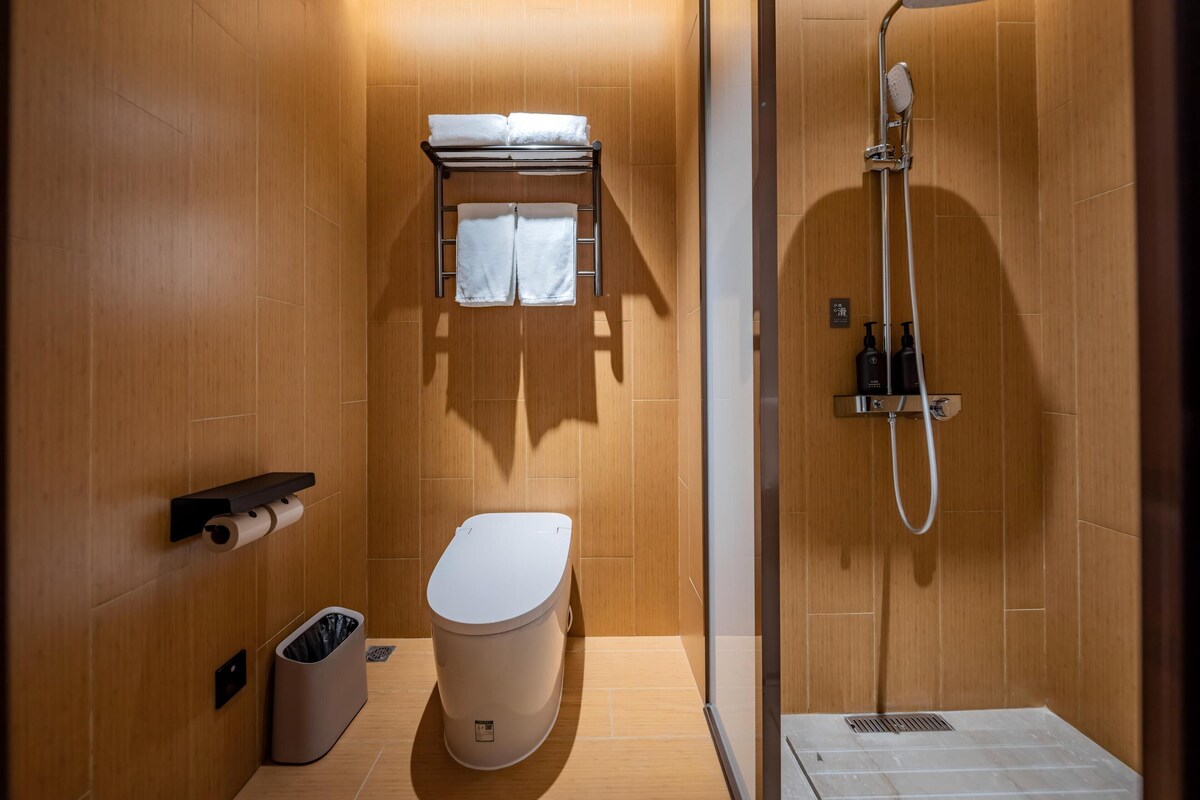 Uma casa de banho moderna com sanita, chuveiro e um porta-toalhas.