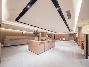 Um hall de hotel moderno com balcão de recepção, área de estar e um grande arranjo de plantas.