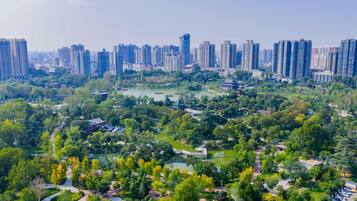 Um parque com caminhos para pedestres, um lago e arquitetura tradicional, integrado a uma paisagem urbana com edifícios altos.