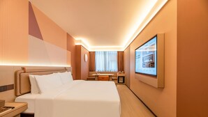 Quarto de hotel com uma cama grande, uma escrivaninha, um espaço de estar e uma televisão na parede.