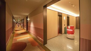 Um corredor de hotel com piso coberto por carpete, portas e uma lixeira.
