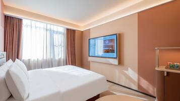 Quarto de hotel com uma cama, televisão fixada na parede e uma mesinha com objetos sobre ela.