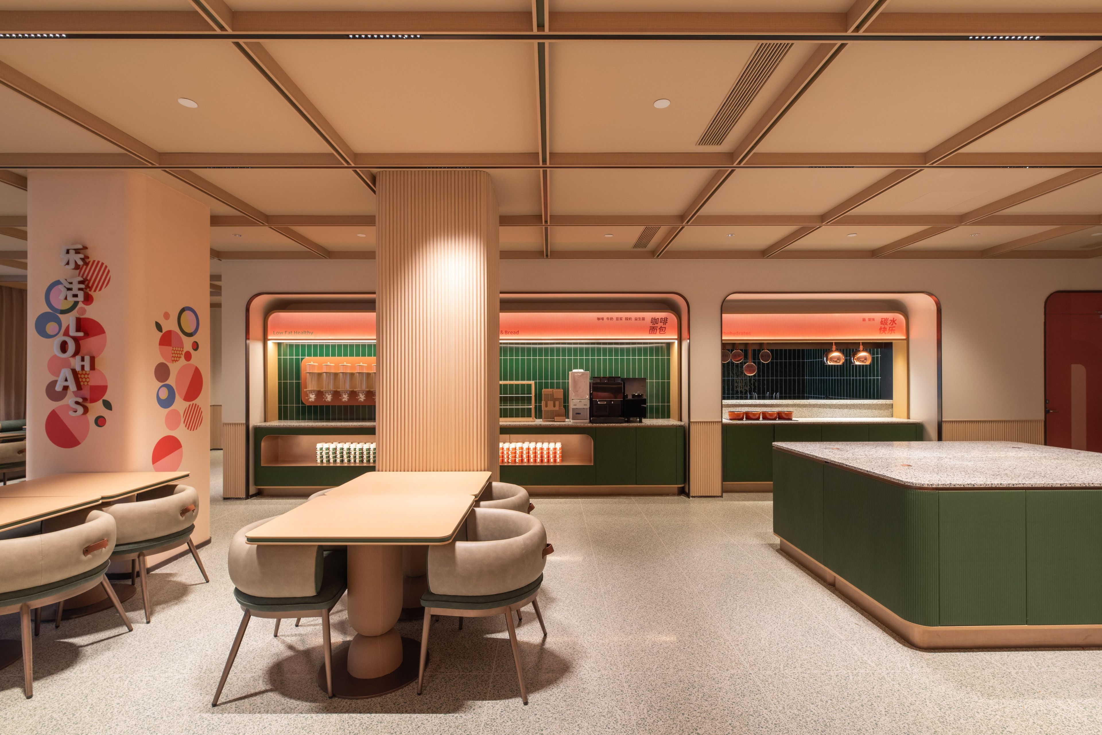 Um interior moderno com uma mesa central e cadeiras, paredes verdes e bege, e duas áreas de balcão com opções de comida e bebida.