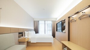Quarto de hotel moderno com cama, sofá, mesa de cabeceira, televisão e guarda-roupa com espelho.