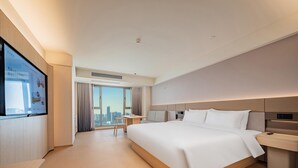 Quarto de hotel moderno com uma cama grande, uma escrivaninha e uma televisão na parede.