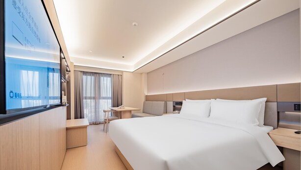 Quarto de hotel moderno com uma cama grande, mesas de cabeceira, escrivaninha e televisão.