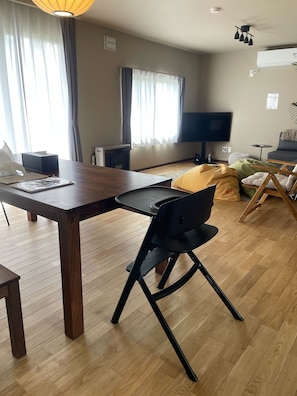 Uma sala de estar moderna com piso de madeira, uma mesa de jantar, uma cadeira preta, um sofá e uma televisão.