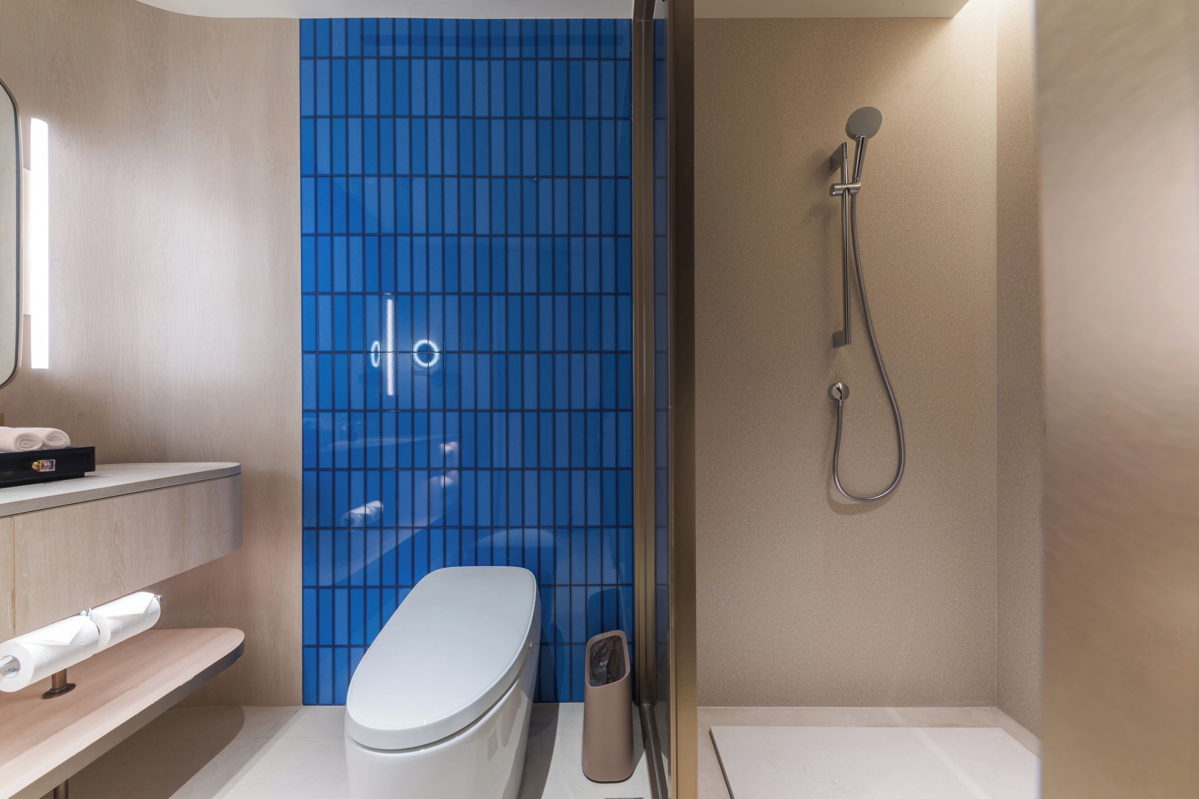 Um banheiro moderno com vaso sanitário, chuveiro e parede revestida de azulejos azuis.
