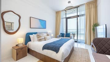 Quarto de hotel moderno com uma cama grande, uma mesinha de cabeceira, uma cadeira, televisão e varanda com vista.