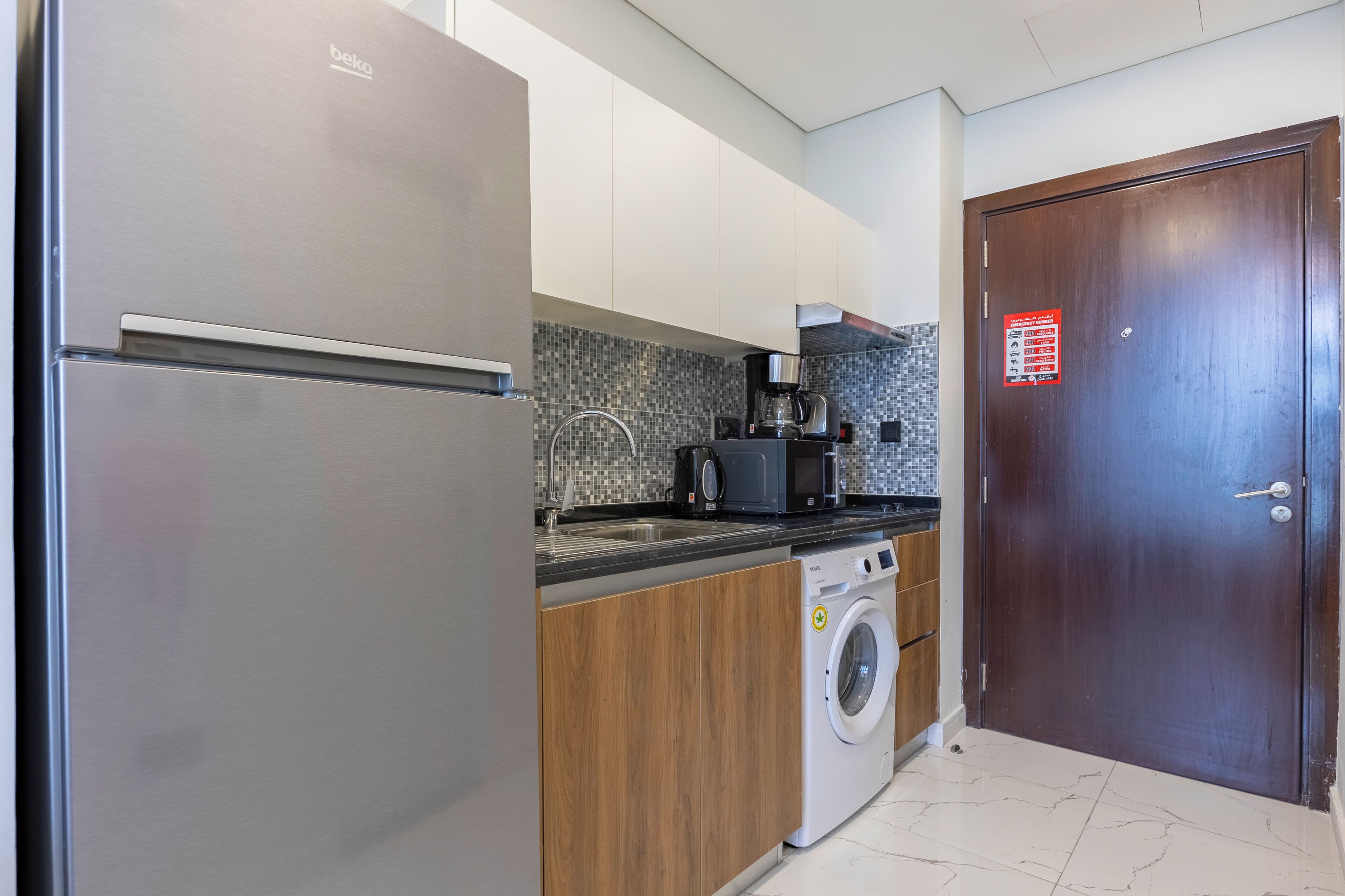 Uma cozinha compacta equipada com geladeira, micro-ondas, cafeteira e máquina de lavar.