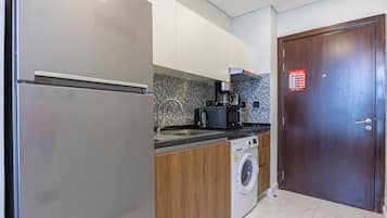 Uma cozinha compacta equipada com geladeira, micro-ondas, cafeteira e máquina de lavar.
