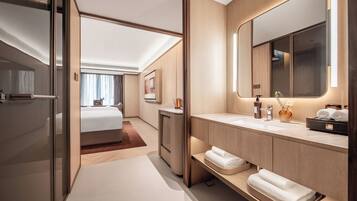 Quarto de hotel moderno com uma cama grande, um banheiro com espelho e um closet espaçoso.