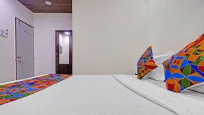 Quarto de hotel com cama, almofadas, uma porta e um corredor.