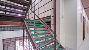Um interior com vários níveis, uma escada, guarda-corpos de metal e chão de azulejos.