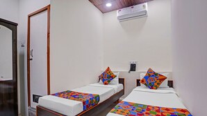 Quarto pequeno e limpo com duas camas de solteiro, uma porta de madeira e um aparelho de ar condicionado na parede.