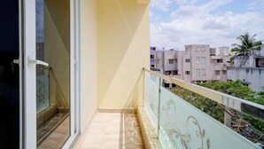 Uma varanda com porta de vidro, guarda-corpo de metal e vista para edifícios vizinhos.