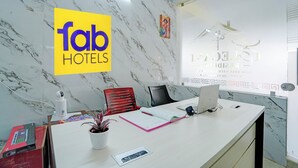 Balcão de recepção de hotel com parede de mármore, placa 'fab hotels', uma planta em vaso, um laptop, um caderno e uma câmera de segurança.