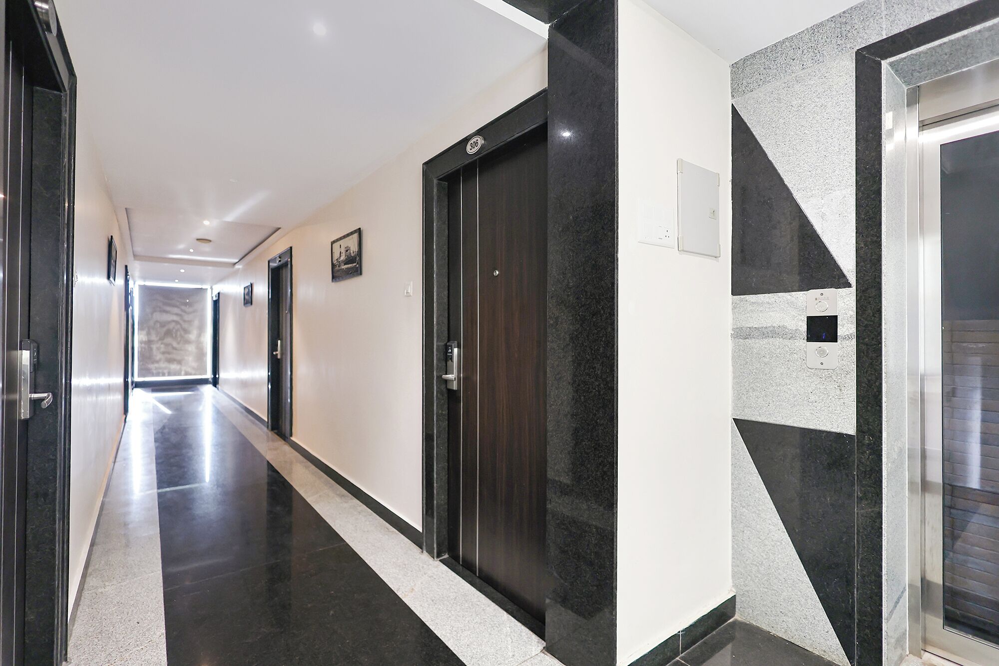Corredor moderno de hotel com portas de madeira escura, piso de mármore e design geométrico na parede.