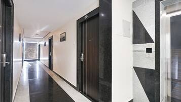 Corredor moderno de hotel com portas de madeira escura, piso de mármore e design geométrico na parede.