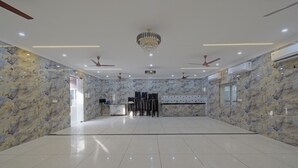 Um hall amplo com paredes de mármore, um candelabro, ventiladores de teto e um balcão de recepção.