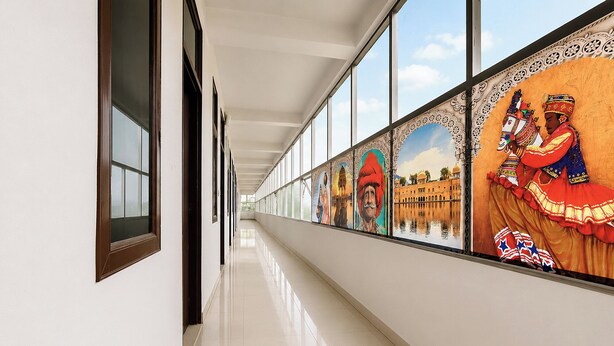 Um corredor longo com grandes janelas e um mural na parede retratando figuras tradicionais.