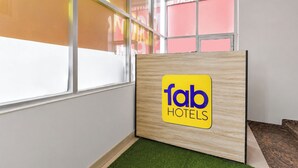Uma área de recepção de hotel com um balcão de madeira, uma placa com a inscrição 'fab hotels' e janelas amplas.