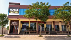 Um hotel com uma placa que diz 'HOTEL PALAK PALACE', apresentando uma fachada moderna com grandes janelas e telhado plano.
