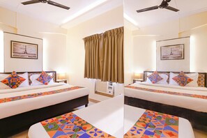 Quarto de hotel com duas camas, um ventilador de teto, uma janela com cortinas e obras de arte nas paredes.