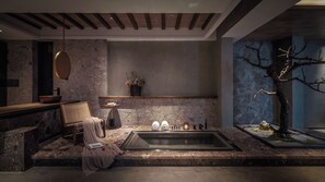 Um banheiro moderno com pia de pedra, um banco de madeira, uma pequena mesa com um vaso e uma escultura de árvore.