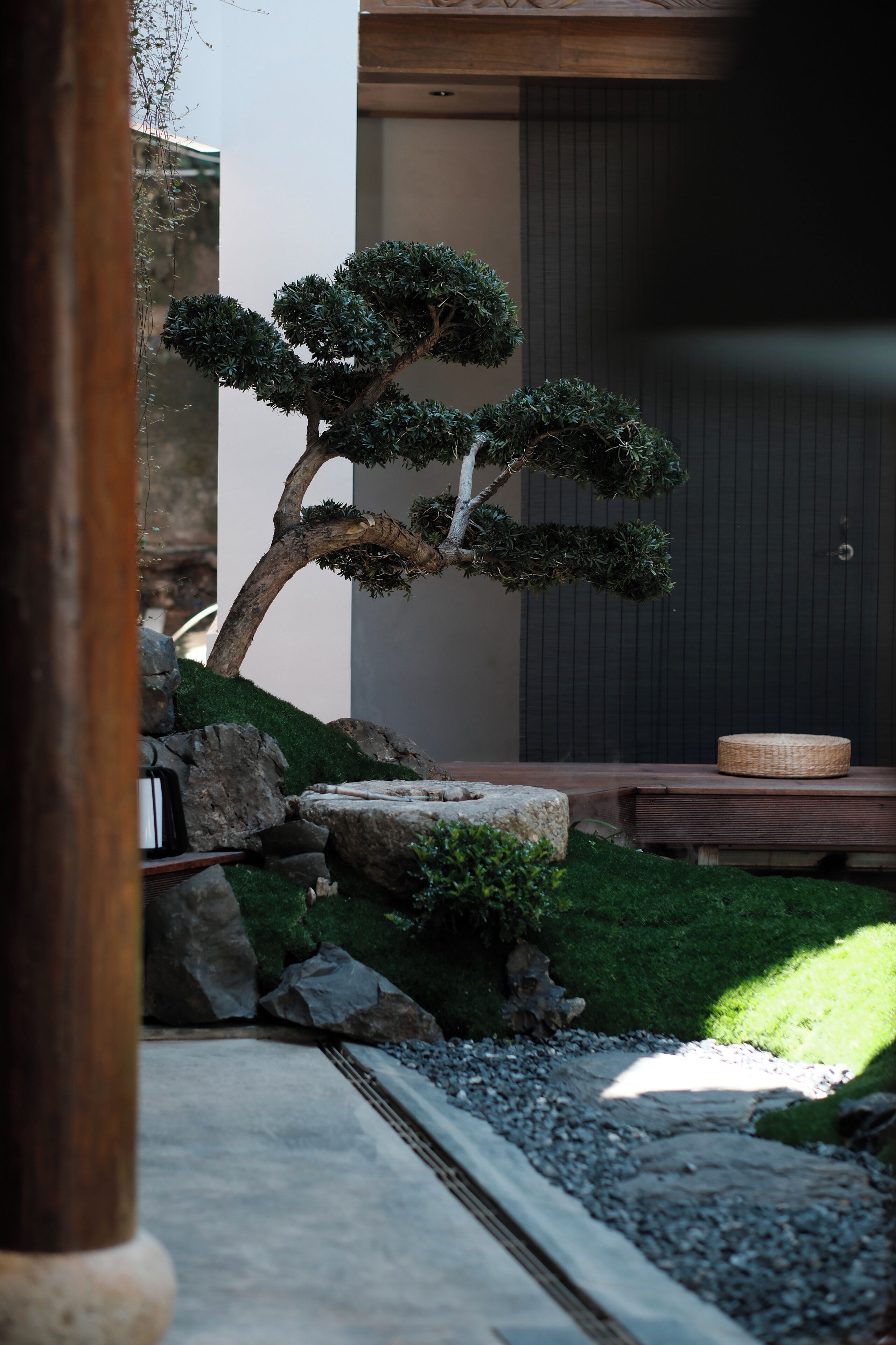 Uma árvore bonsai em um jardim com pedras, um banco de madeira e uma cesta de vime.