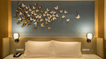Quarto de hotel com cama, duas luminárias de apoio, telefone fixado na parede e arte decorativa de borboleta.