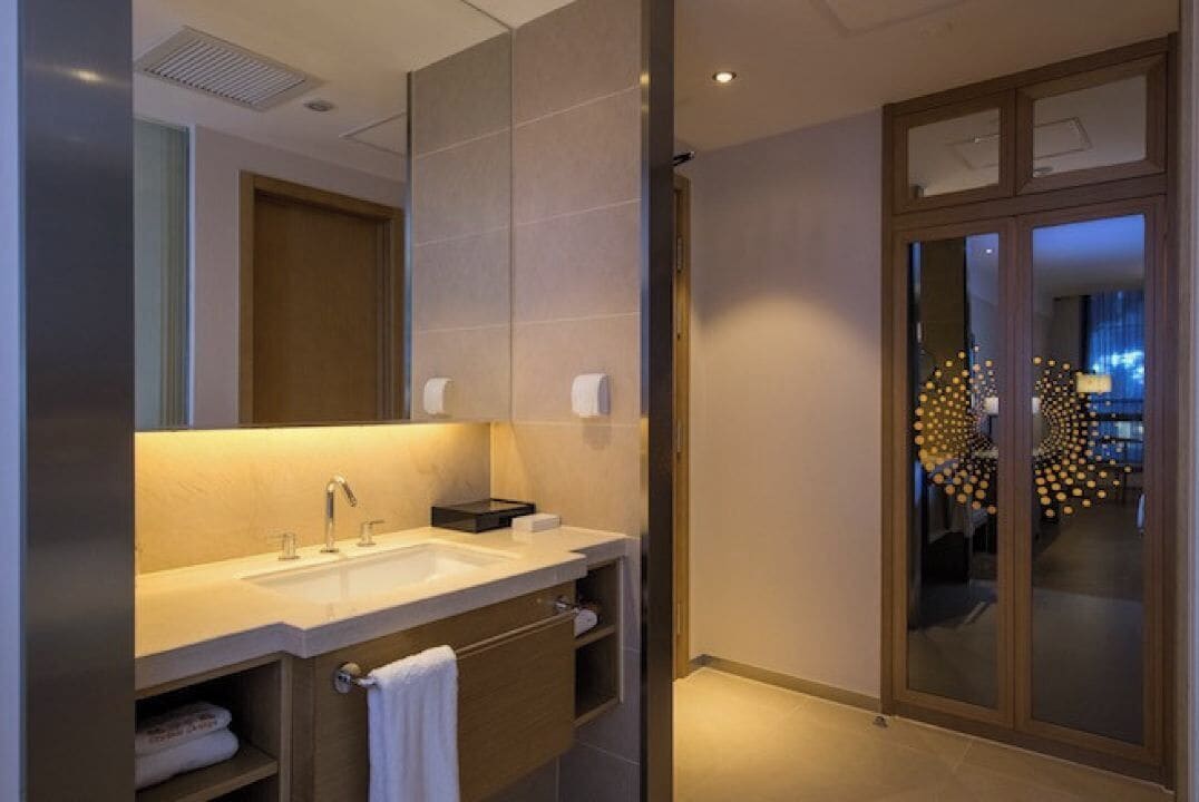 Uma casa de banho moderna com um espelho grande, uma pia e uma porta de vidro que dá para uma área de refeições.