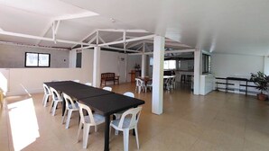 Um quarto espaçoso com uma mesa comprida e cadeiras, uma área de cozinha e uma varanda.