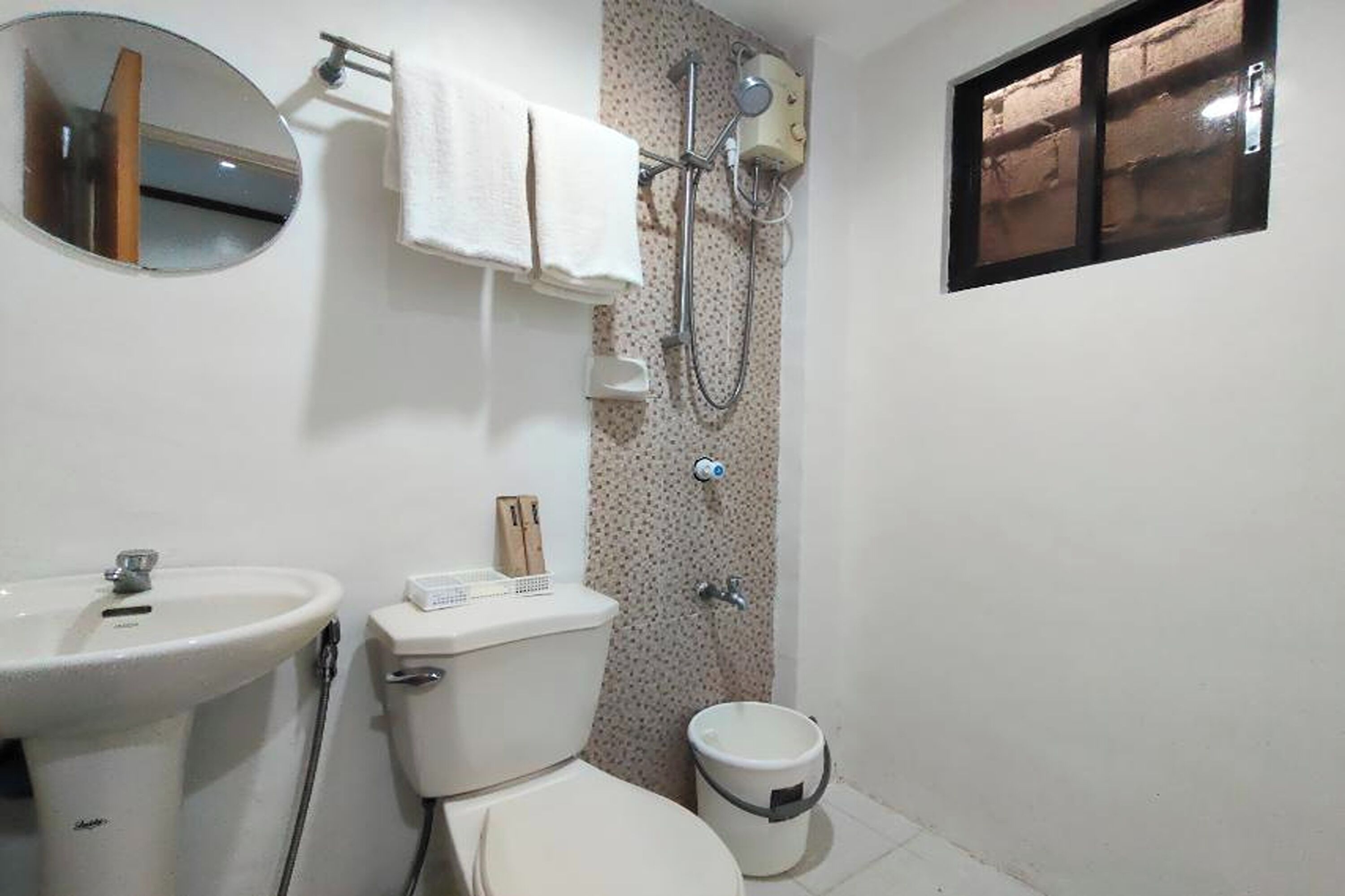 Casa de banho com lavatório, sanita, chuveiro e uma pequena janela.