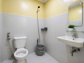 Casa de banho com sanita, chuveiro, lavatório e uma pequena planta em vaso sobre o espelho.