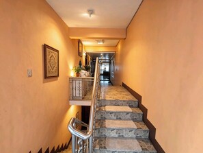 Escada com degraus de pedra e corrimão de metal, levando a um patamar com planta em vaso e obra de arte emoldurada.