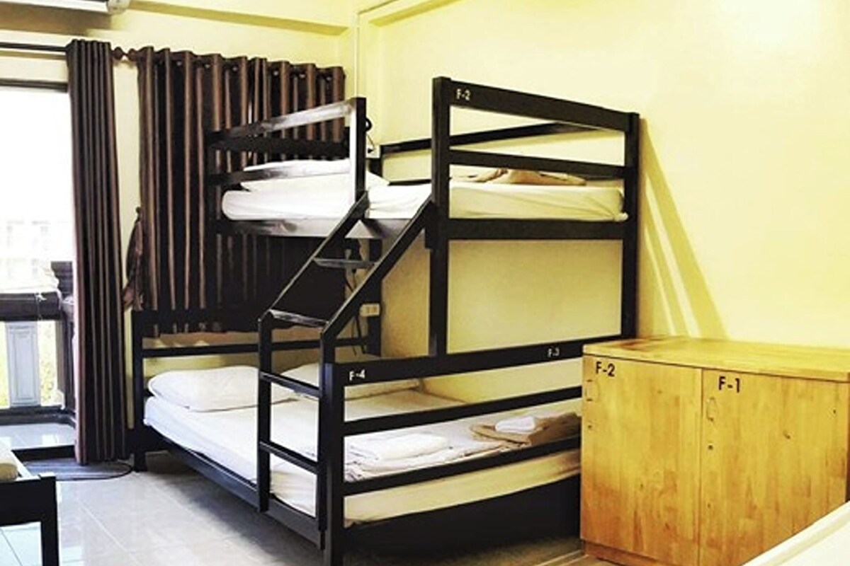 Uma cama de beliche com três andares, um armário de madeira e uma janela com cortinas.