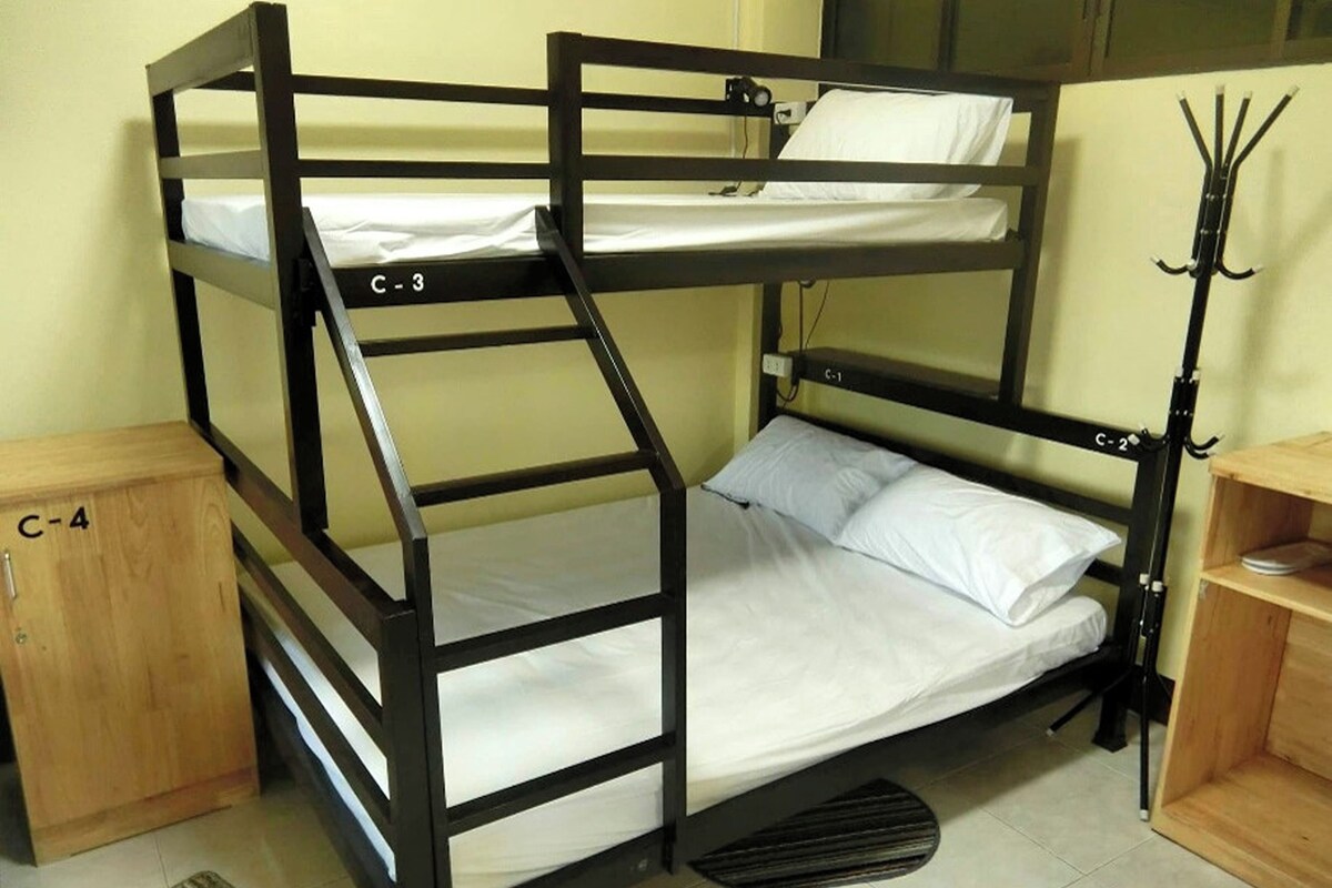Uma cama beliche com três níveis, identificados como C-1, C-2 e C-3, em um quarto com um armário de madeira e um cabideiro.