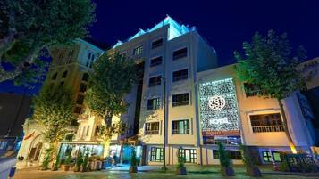 Um hotel com vários andares, um letreiro iluminado chamativo, área de estar ao ar livre e árvores ao redor.