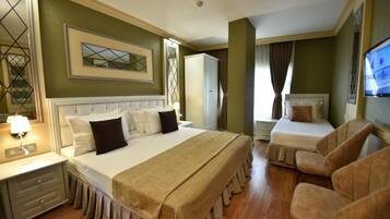 Quarto de hotel com uma cama grande, uma cama menor, uma escrivaninha, uma cadeira e uma televisão.