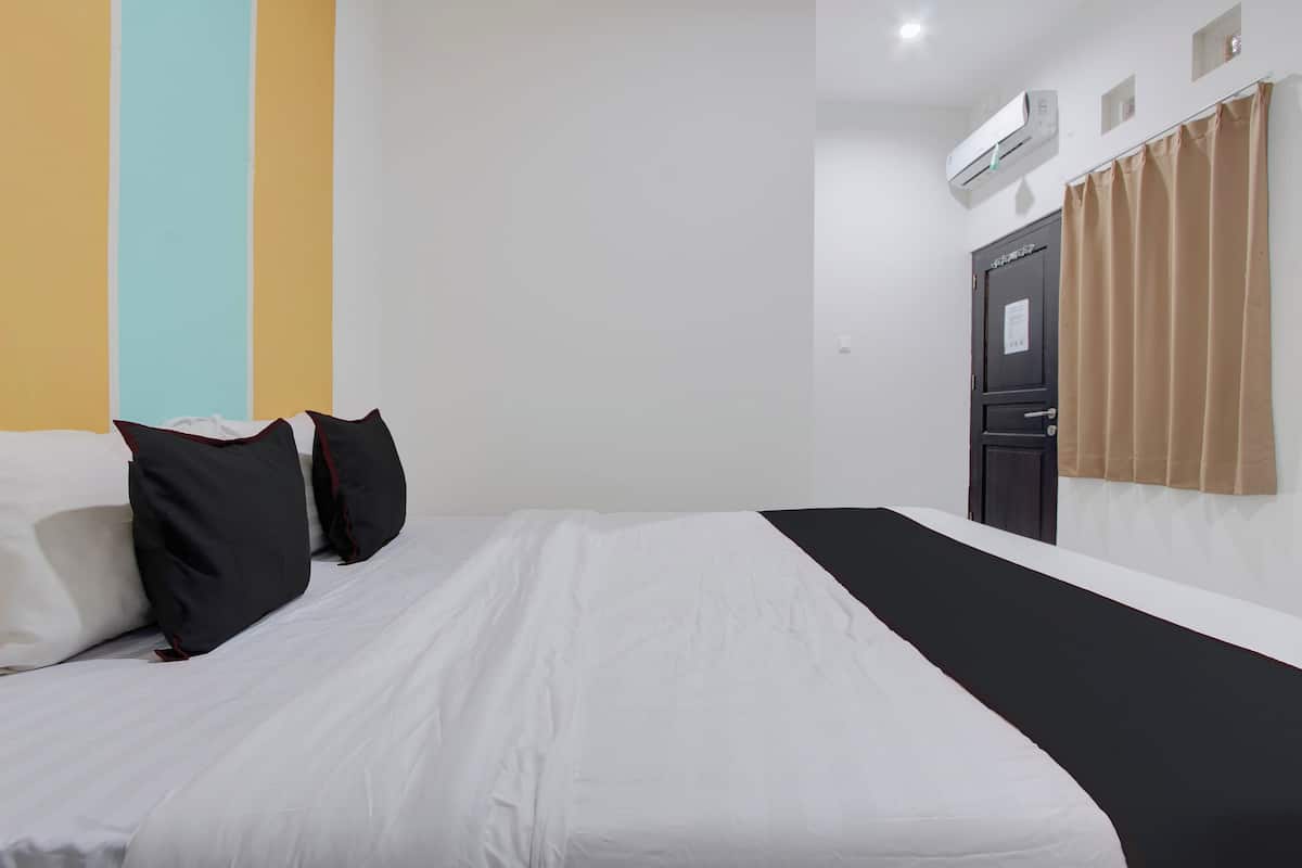 Quarto de hotel com cama, almofadas, mesa de cabeceira preta, guarda-roupa e ar condicionado.