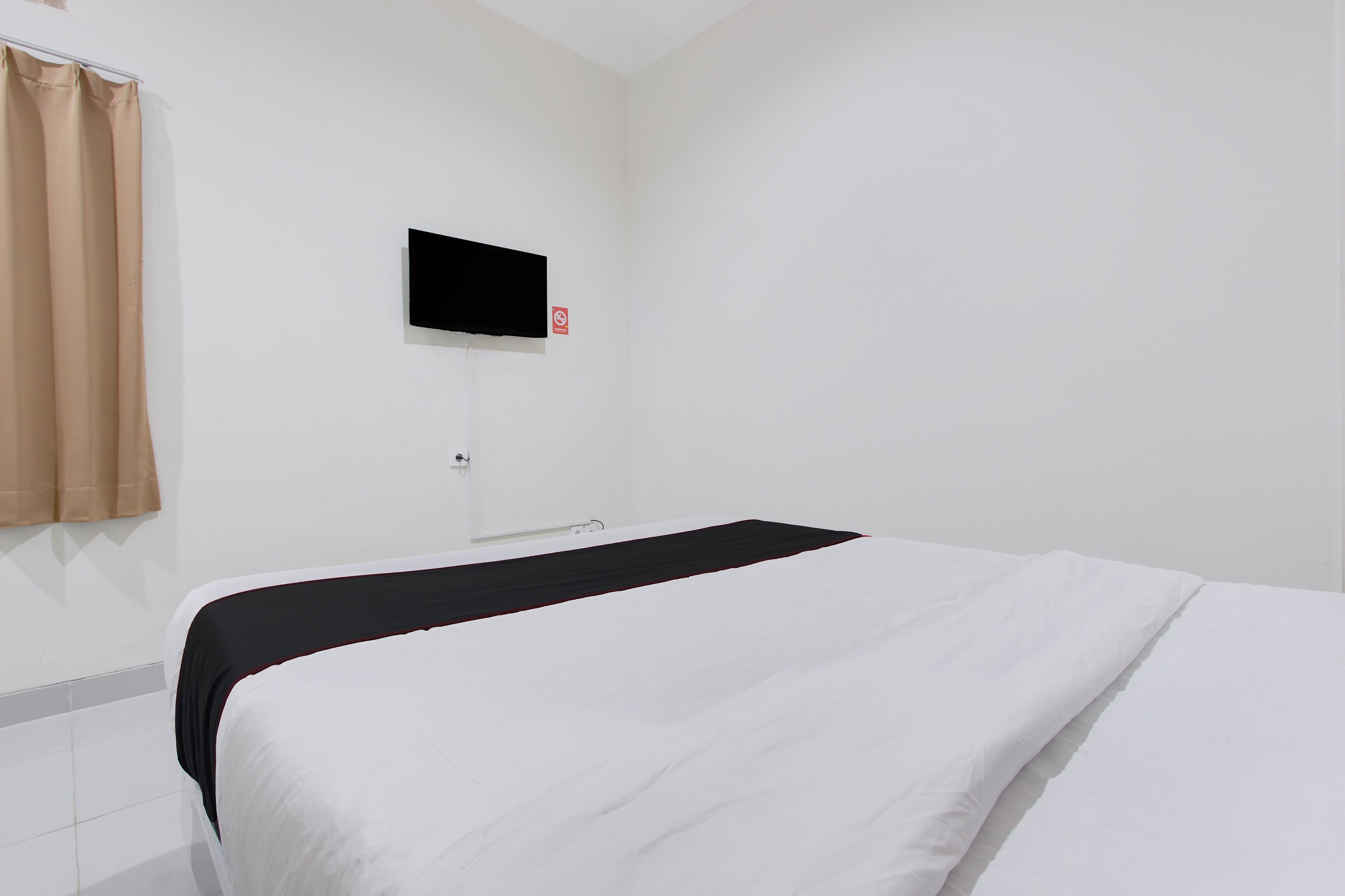 Quarto de hotel minimalista com uma cama, televisão fixada na parede e cortina na janela.