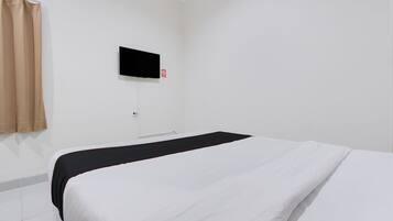 Quarto de hotel minimalista com uma cama, televisão fixada na parede e cortina na janela.