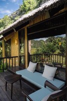 Um deck de madeira com telhado de palha, área de estar ao ar livre e vista para a paisagem natural.