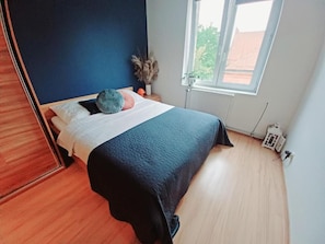 Quarto com cama, janela, radiador e piso de madeira.