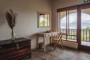 Quarto com cômoda de madeira, escrivaninha com gavetas, cadeira, espelho e uma janela grande com vista.